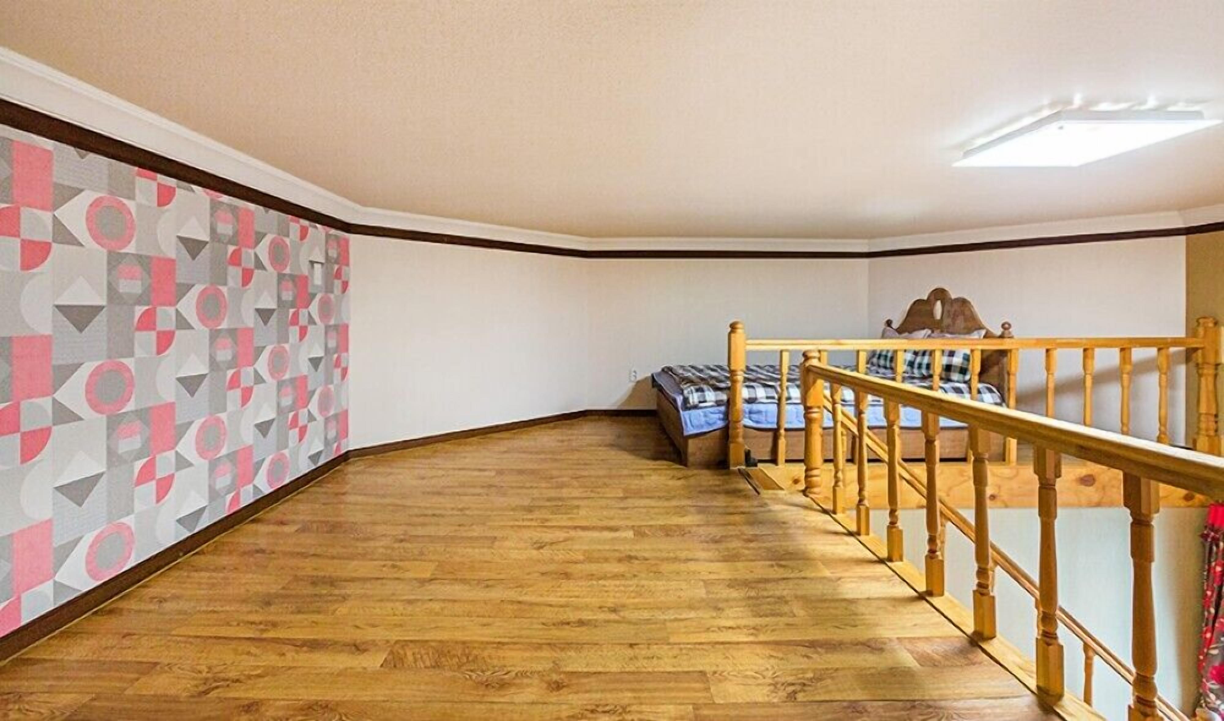 Quarto com chão de madeira, uma cama com cabeceira de madeira e papel de parede estampado em uma parede.