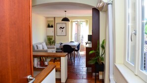 Um corredor estreito que leva a uma sala de jantar com mesa e cadeiras, um sofá e um quadro na parede.