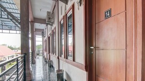 Um corredor com piso ladrilhado, porta de madeira com o número 14 e corrimão de metal à esquerda.