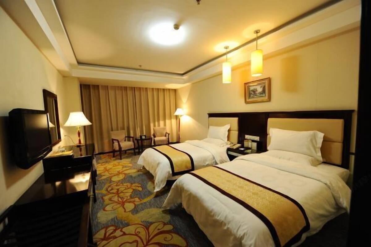 Quarto de hotel com duas camas, televisão, escrivaninha e uma cadeira.