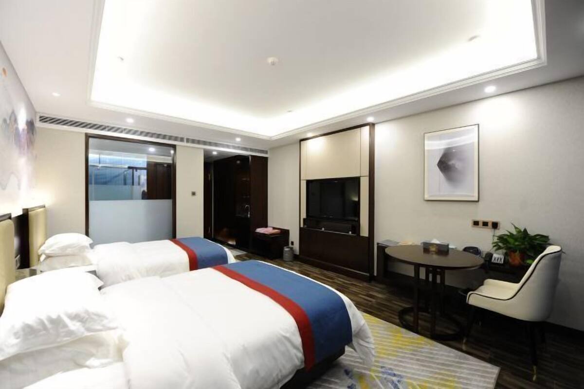 Quarto de hotel com duas camas, uma mesa, uma cadeira, uma TV e uma pequena mesa.
