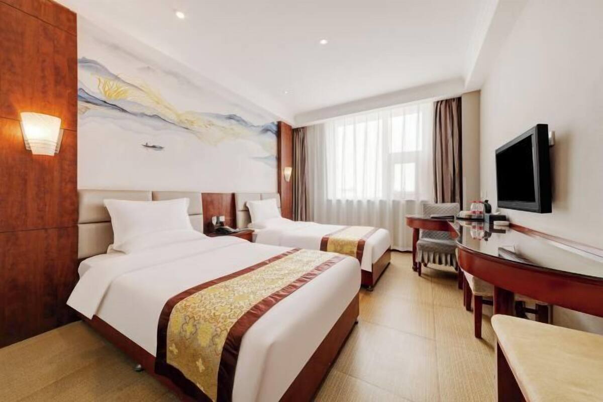 Quarto de hotel com duas camas, uma escrivaninha, televisão e um quadro na parede.