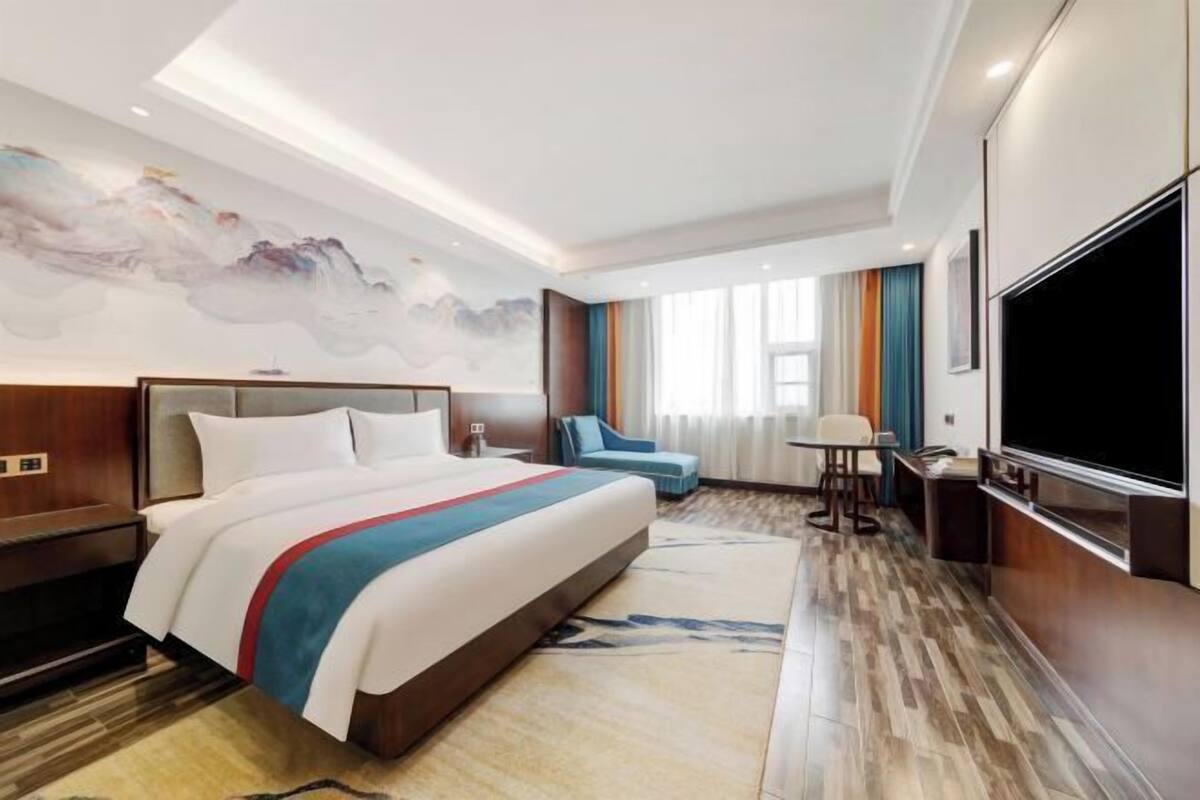 Quarto de hotel com uma cama grande, televisão de tela plana, escrivaninha e uma cadeira.