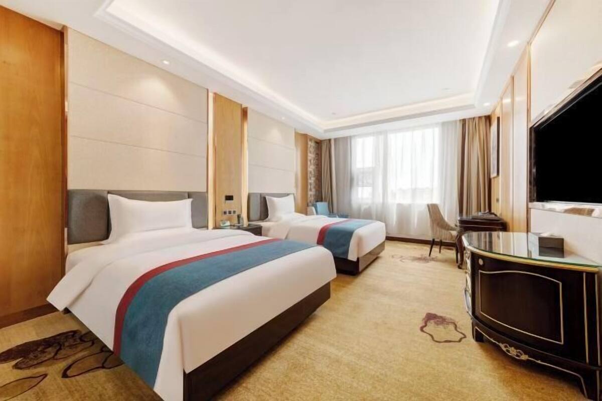 Quarto de hotel com duas camas, televisão, escrivaninha e uma janela grande.