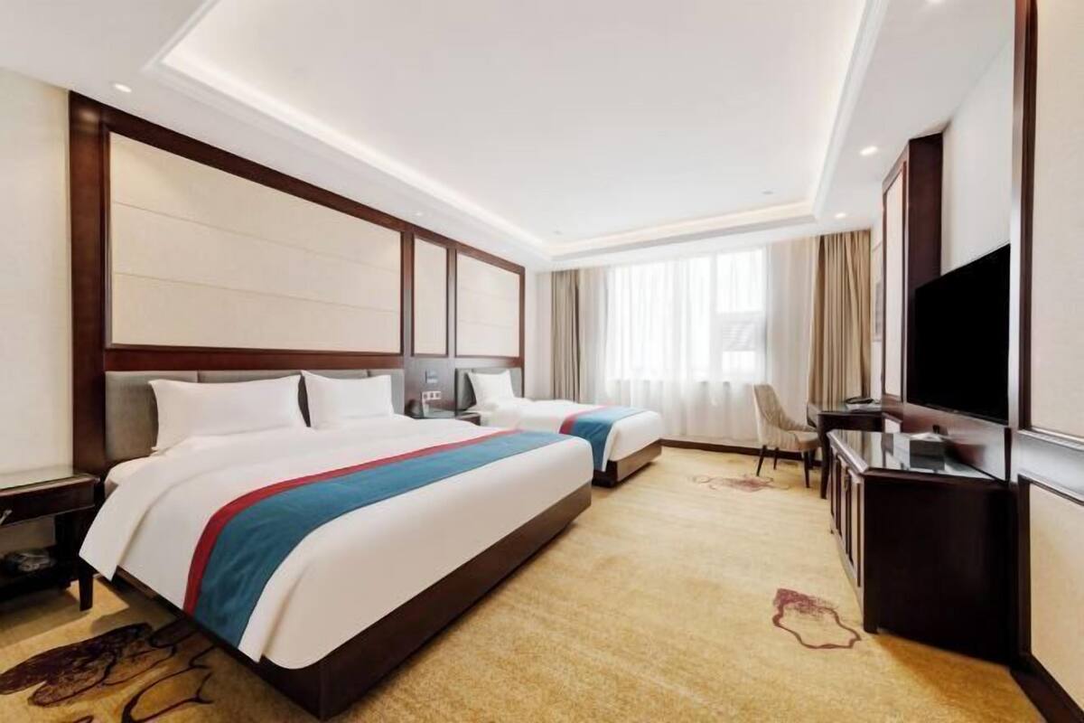 Quarto de hotel com duas camas, televisão, escrivaninha e uma janela grande.