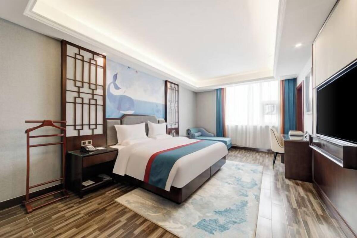 Quarto de hotel moderno com uma cama grande, uma escrivaninha, uma televisão e vista para a cidade.