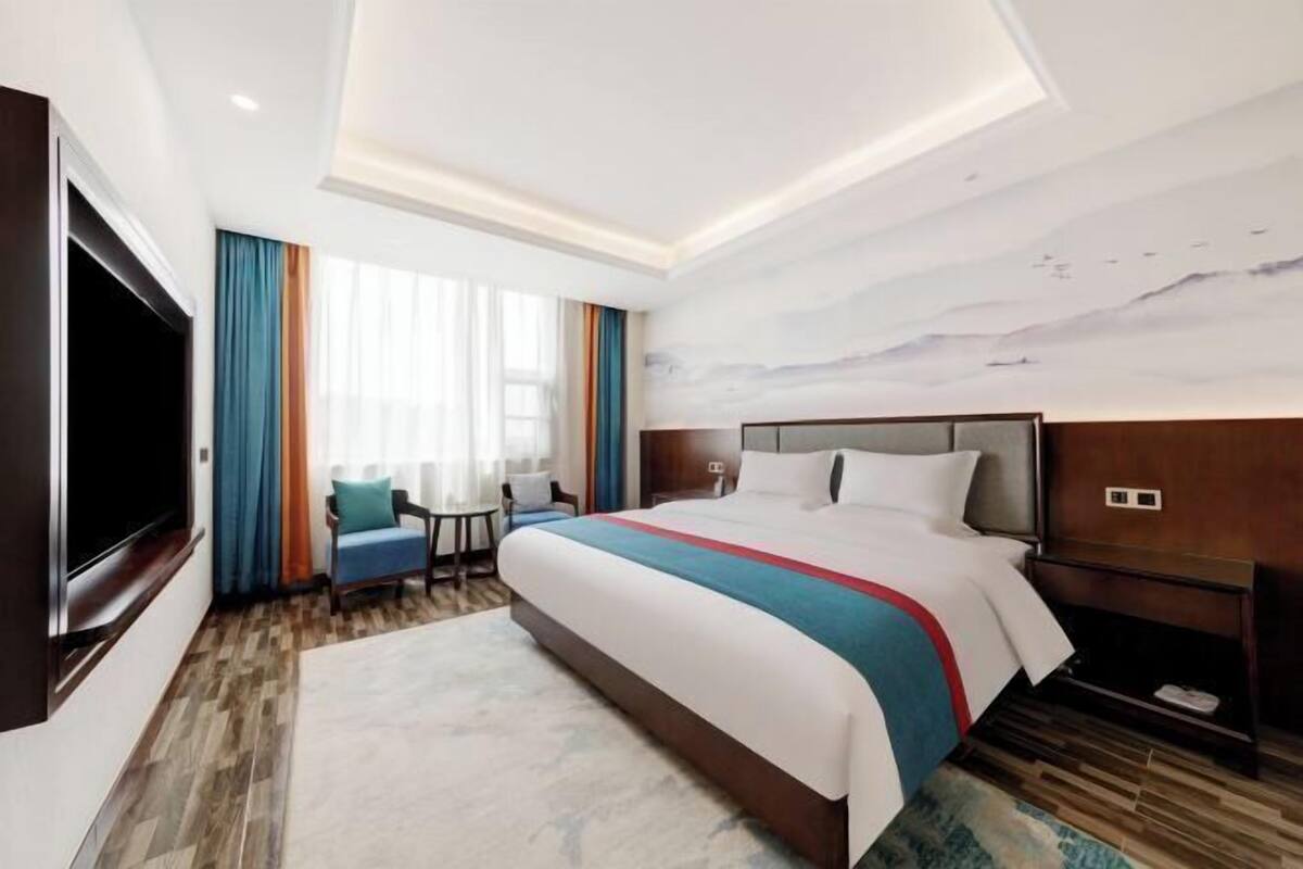 Quarto de hotel com cama grande, televisão de tela plana, mesinha e cadeira.