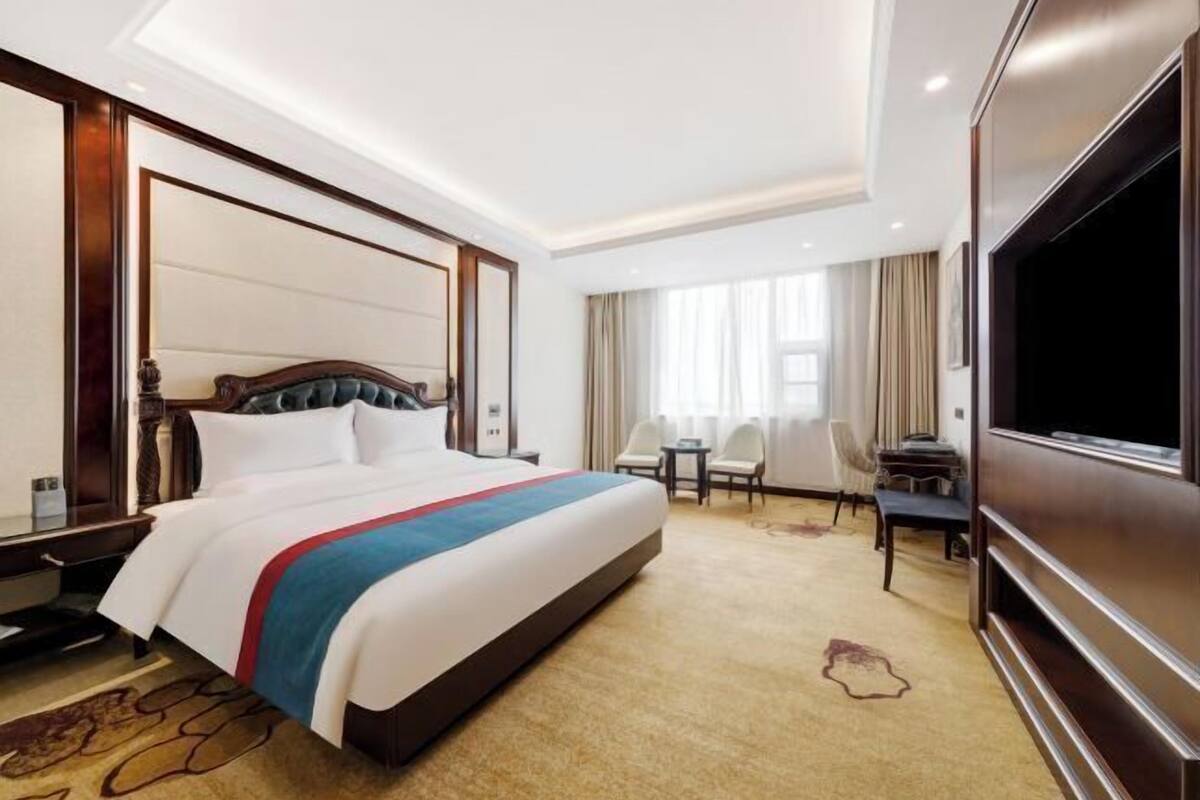 Quarto de hotel com uma cama grande, uma escrivaninha, uma cadeira, uma televisão e uma janela com cortinas.