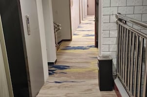 Corredor com piso estampado, portas à esquerda e lixeira à direita.