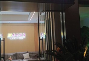 Interior de hotel com balcão de recepção, sofá e planta.