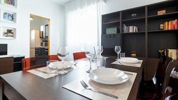 Uma área de refeições com uma mesa de madeira posta para dois, dois copos de vinho, dois copos de água e um garfo sobre um jogo americano.