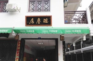 Entrada de hotel com toldo verde, uma placa com caracteres chineses e estilo arquitetônico tradicional.