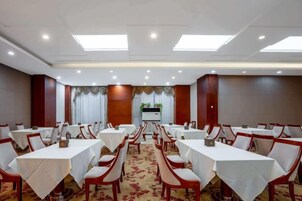 Sala de conferência com várias mesas e cadeiras, piso coberto por carpete e decoração em tons neutros.
