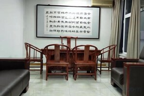 Quarto com uma mesa de jantar e cadeiras, um sofá e uma tela na parede exibindo texto.