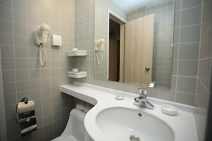 Casa de banho com uma pia branca, um espelho, um porta-toalhas e um secador de cabelo na parede.