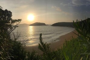 Uma praia com águas calmas, areal arenoso e colinas ao longe.