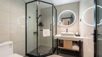 Casa de banho moderna com chuveiro separado por vidro, lavatório branco e espelho com luzes circulares.