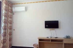 Quarto com televisão fixada na parede, um armário de madeira abaixo e um aparelho de ar condicionado na parede.