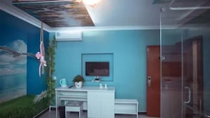 Quarto com parede verde-água, escrivaninha branca com televisão, cadeira suspensa rosa e porta de vidro.