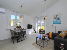 Uma sala de estar moderna com área de jantar, um sofá, uma mesa de centro e uma TV na parede.