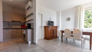 Cozinha moderna com forno embutido, área de refeições com mesa e cadeiras de madeira, e uma TV sobre um suporte.