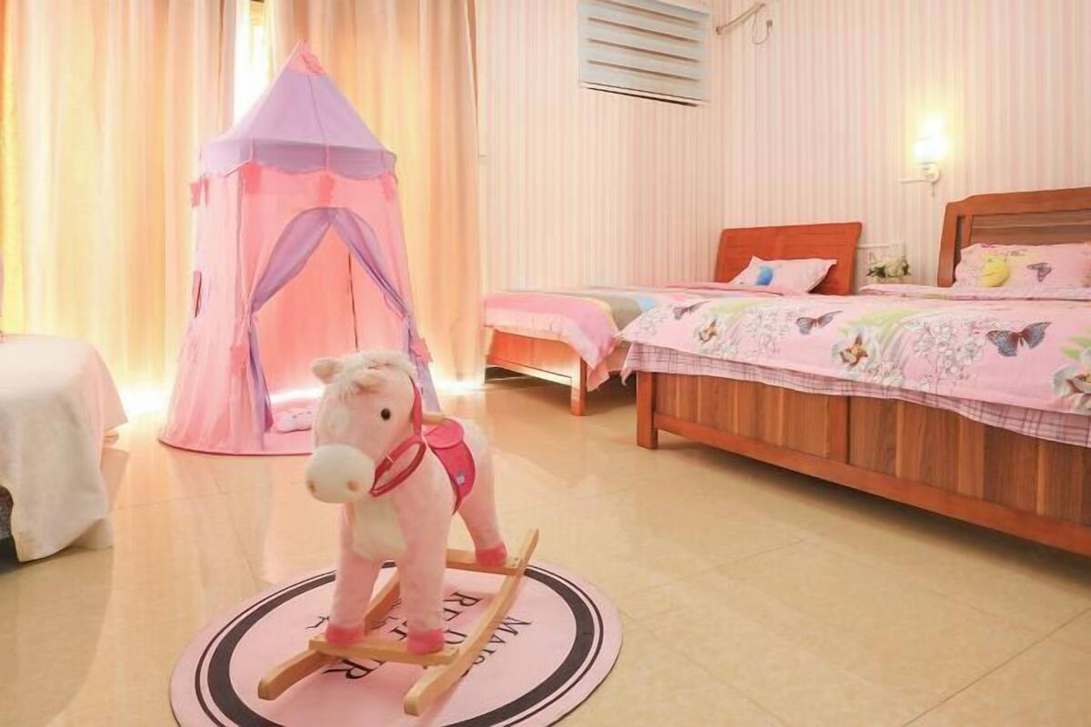 Quarto infantil com uma tenda rosa, um cavalinho de balanço, duas camas com roupa de cama rosa e cabeceiras de madeira.