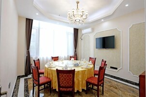 Uma área de refeições com uma mesa redonda, cadeiras estofadas em vermelho, um lustre e uma TV de tela plana na parede.
