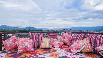 Área de estar no terraço com almofadas estampadas e vista para montanhas.