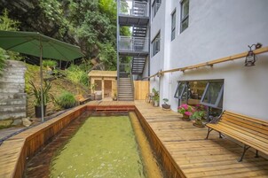 Um deck de madeira com uma piscina pequena, um banco e uma escadaria que leva a um andar superior.