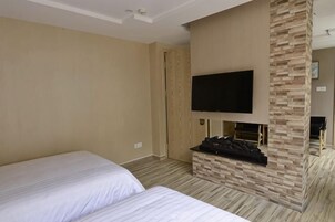 Quarto de hotel com duas camas, televisão de tela plana na parede e lareira.