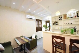 Uma área de refeições com mesa e cadeiras, um bar com prateleiras cheias de garrafas e uma janela com vista.