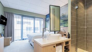 Quarto de hotel com cama, toucador de madeira com pia, espelho grande e área de chuveiro.