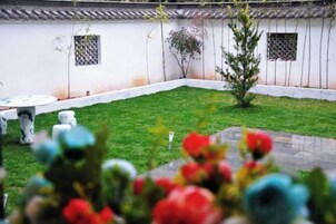 Pátio com uma pequena árvore, piso de azulejos e parede branca com uma janela.
