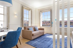 Uma sala de estar moderna com um sofá bege, poltronas azuis e uma grande janela com vista para a cidade.