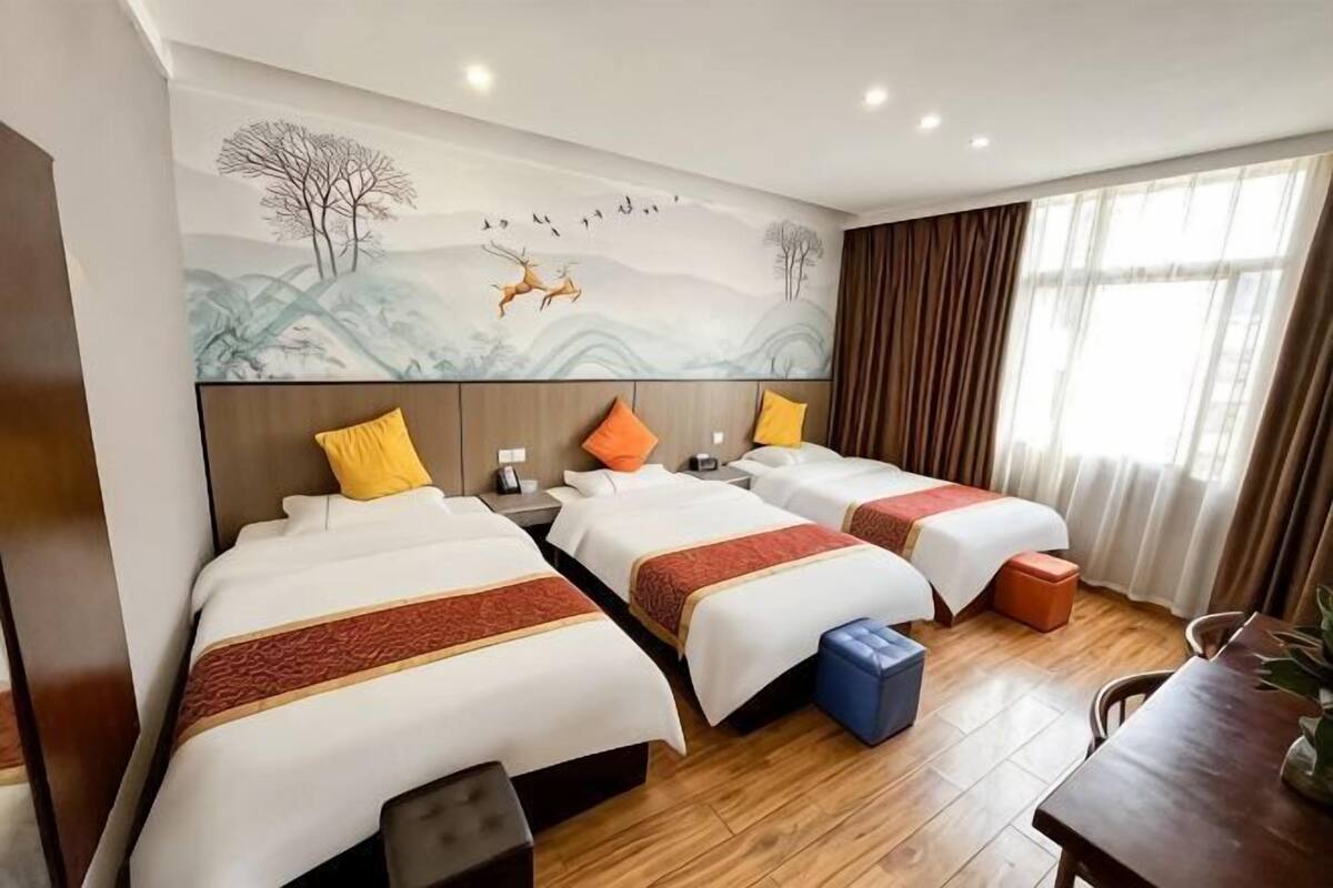 Quarto de hotel com duas camas, piso de madeira, um mural na parede e uma janela com cortinas.
