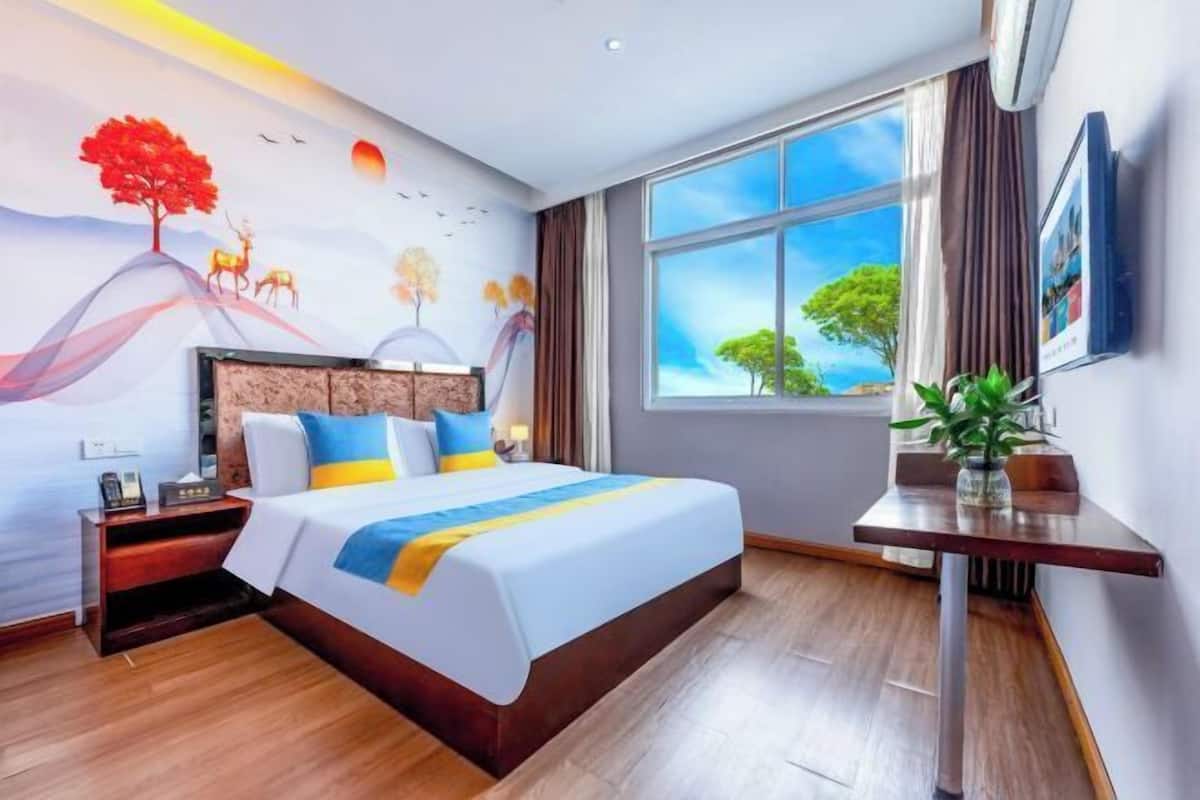 Quarto de hotel com cama, mesa de cabeceira, janela com vista e um mural na parede.