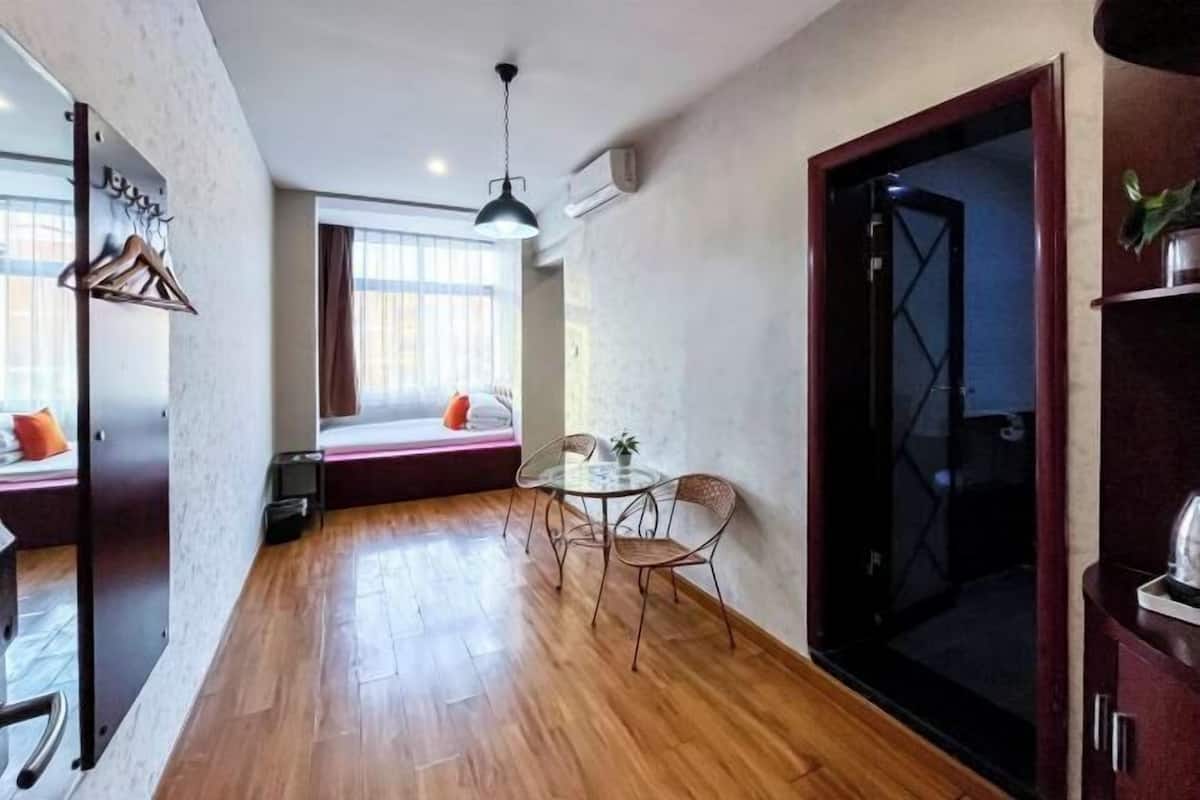 Um quarto com piso de madeira, uma mesa redonda de vidro com cadeiras, um lustre pendente, uma porta deslizante e um porta-roupas fixado na parede.