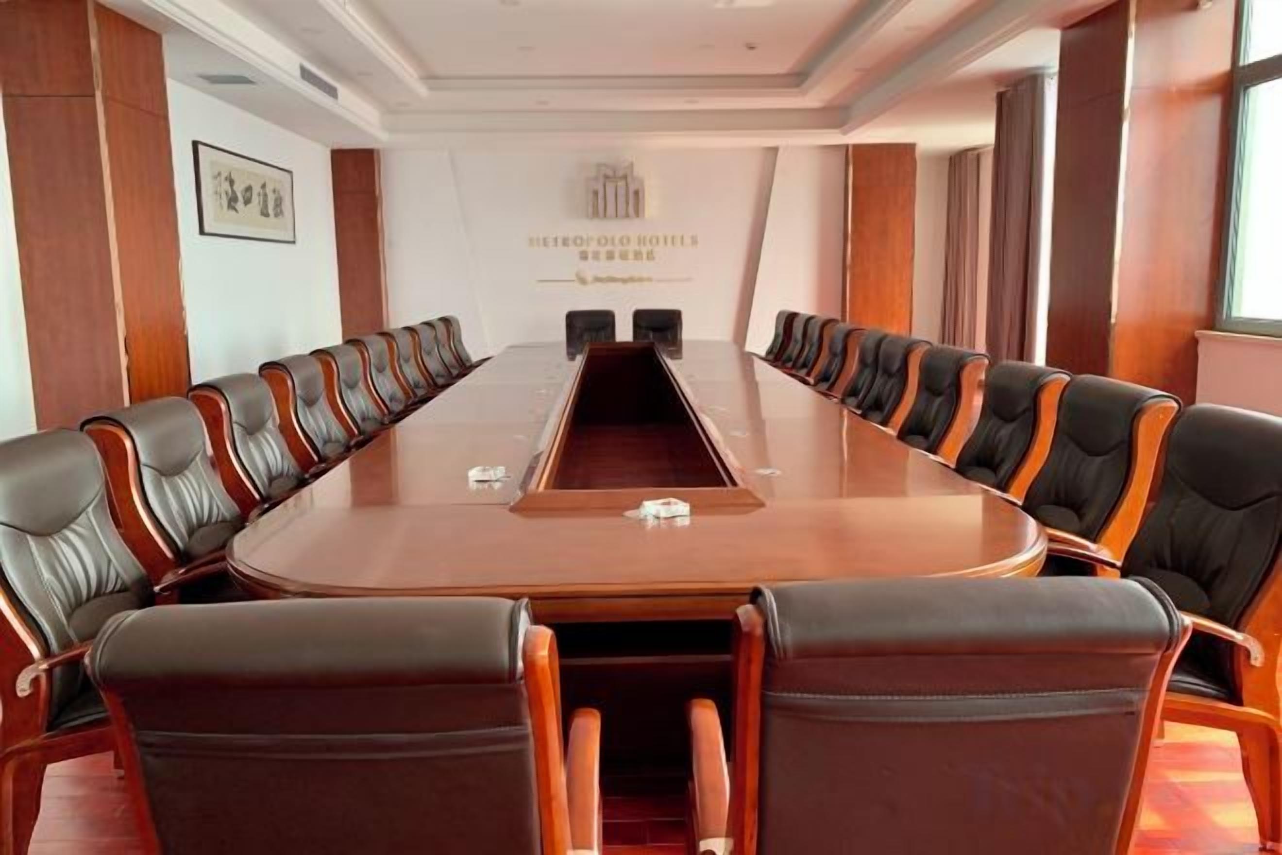 Uma sala de conferências com uma mesa comprida e várias cadeiras, um logotipo na parede e uma janela que oferece iluminação natural.