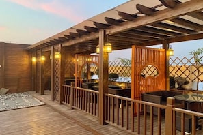 Um deck de madeira ao ar livre com pérgola,  área de estar e um pequeno elemento aquático.