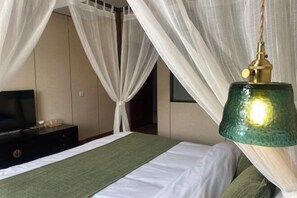 Quarto com cama, televisão sobre uma cômoda e luminária pendente verde.