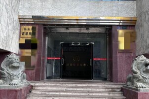 Entrada de edifício com fachada de mármore, estátuas de leões de cada lado e um letreiro sobre a porta.