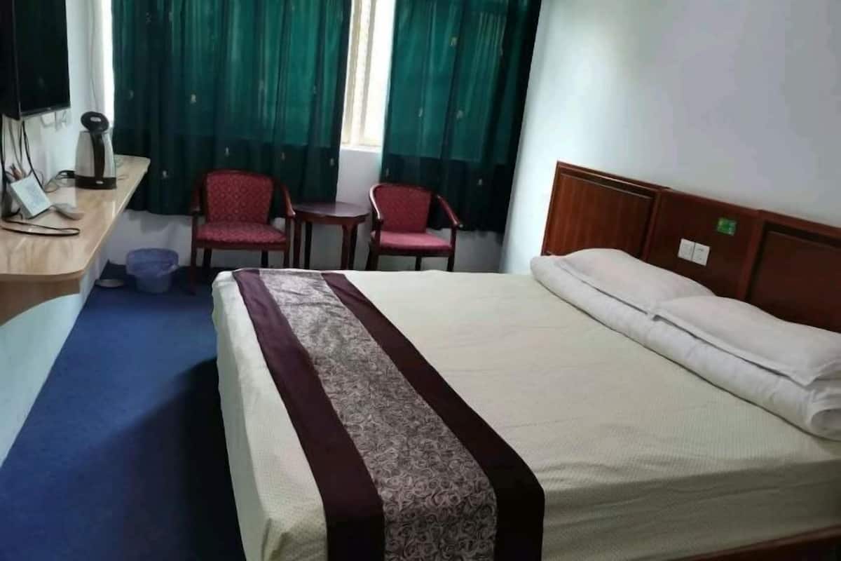 Quarto de hotel com cama, escrivaninha com cadeira, mesinha e janela com cortinas.