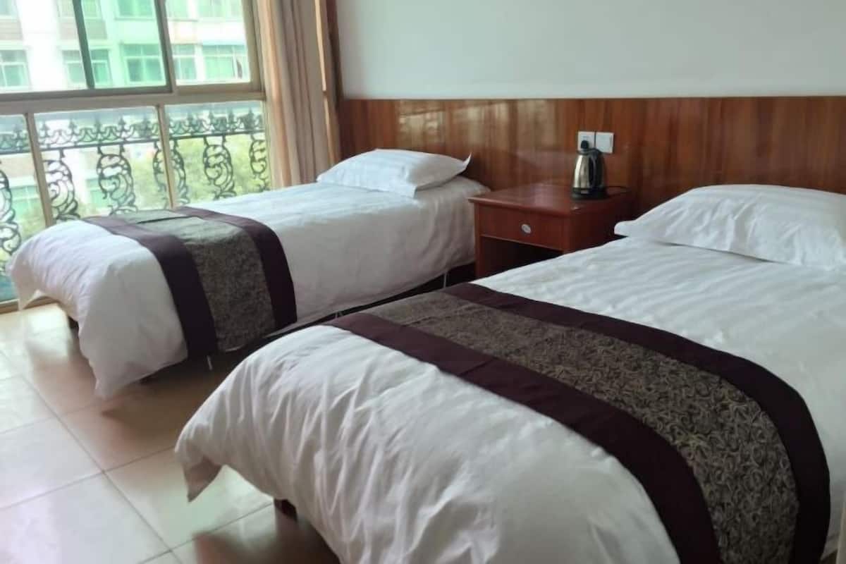 Quarto de hotel com duas camas, cabeceira de madeira, mesa de cabeceira com chaleira e vista para uma varanda com corrimão.