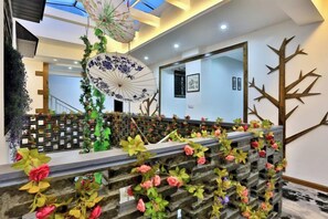 Recepção com parede de pedra decorada com flores, escada e um espelho grande.