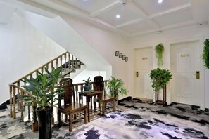 Um hall de hotel com escadas, móveis de madeira, plantas em vasos e um tapete estampado.