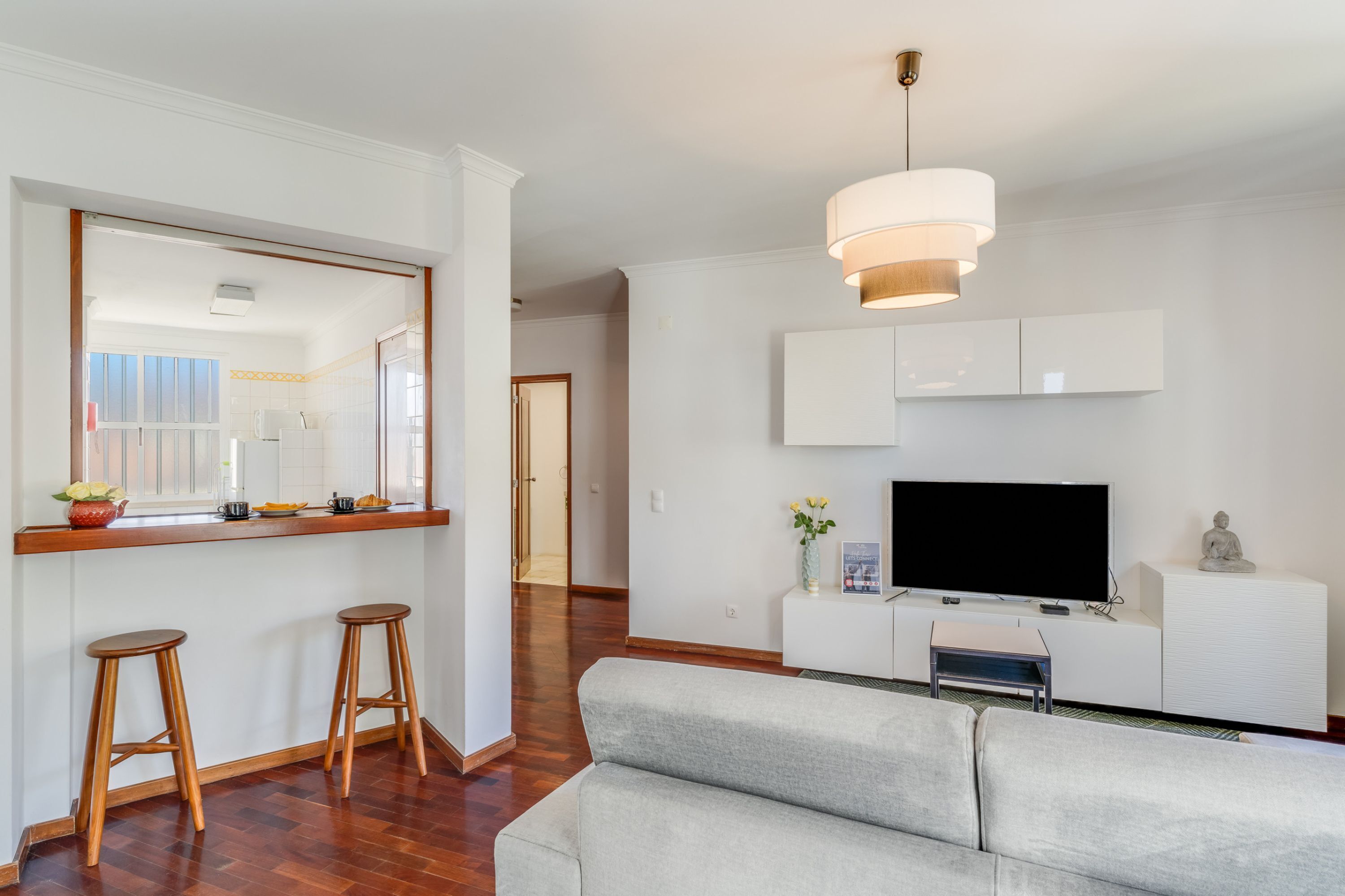 Uma sala de estar moderna com uma grande televisão de tela plana, um sofá, banquetas de madeira e uma área de jantar com balcão e banquetas de madeira.