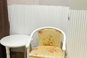 Uma cadeira branca com almofada floral e uma pequena mesa branca ao lado.