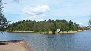 Vista para o lago com uma praia de areia e uma placa ao longe.