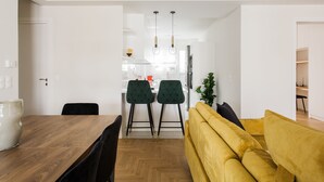 Uma cozinha moderna com armários brancos, uma mesa de jantar de madeira, duas cadeiras estofadas verdes e um sofá amarelo.
