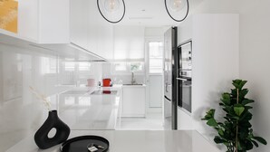 Cozinha moderna com armários brancos, uma ilha central e uma geladeira.